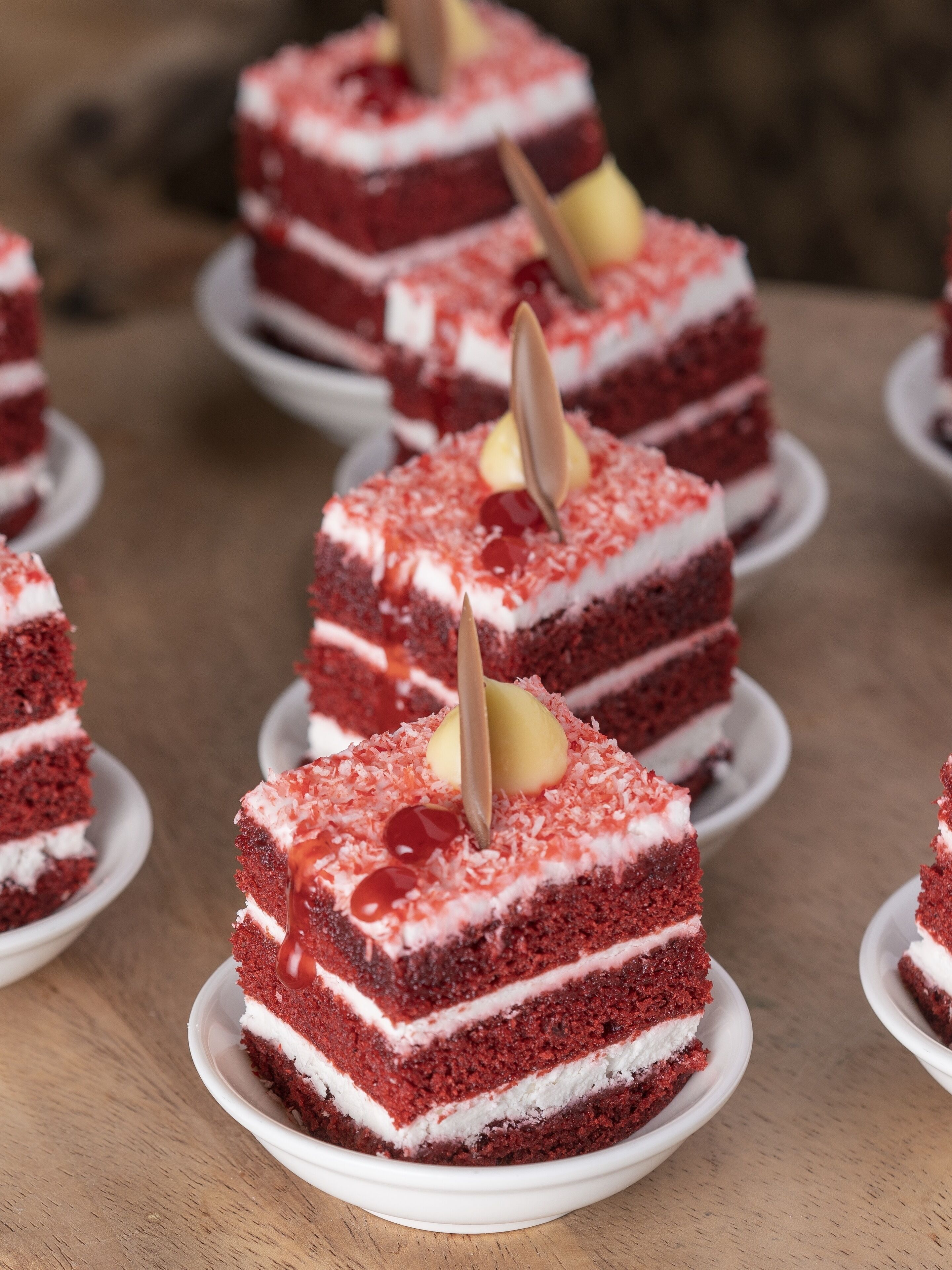 Fatias de bolo quadrado de veludo vermelho com cobertura branca e cereja em um prato branco.