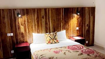 Quarto com cabeceira de madeira, cama com roupa de cama floral, duas mesas de cabeceira e um aparelho de ar condicionado na parede.