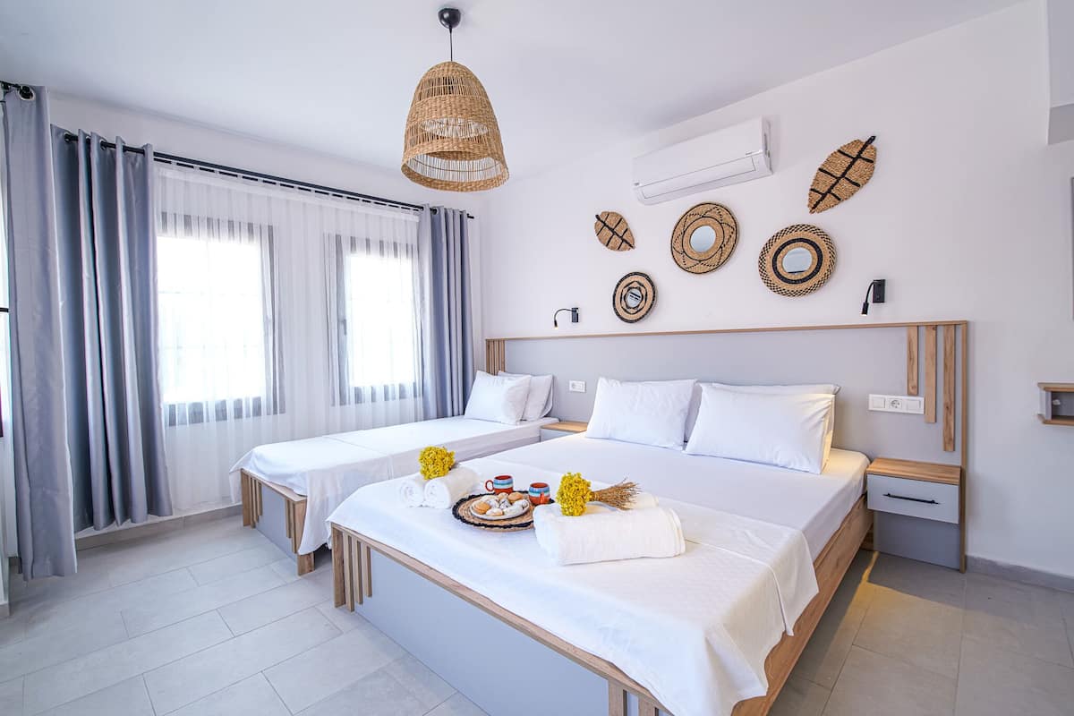 Quarto de hotel com duas camas, uma mesa de cabeceira, luminária e ar condicionado fixado na parede.