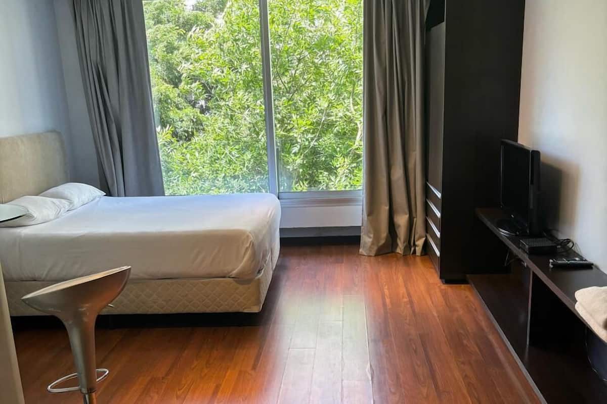 Quarto de hotel moderno com cama, escrivaninha, cadeira, televisão e uma janela ampla com cortinas.