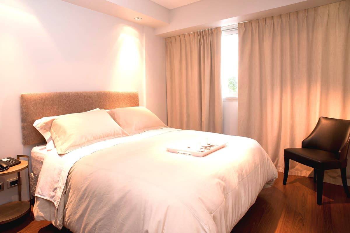 Uma cama bem arrumada com cabeceira, mesa de cabeceira e uma cadeira.
