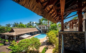 Um resort com piscina, construções de palha e vegetação exuberante.