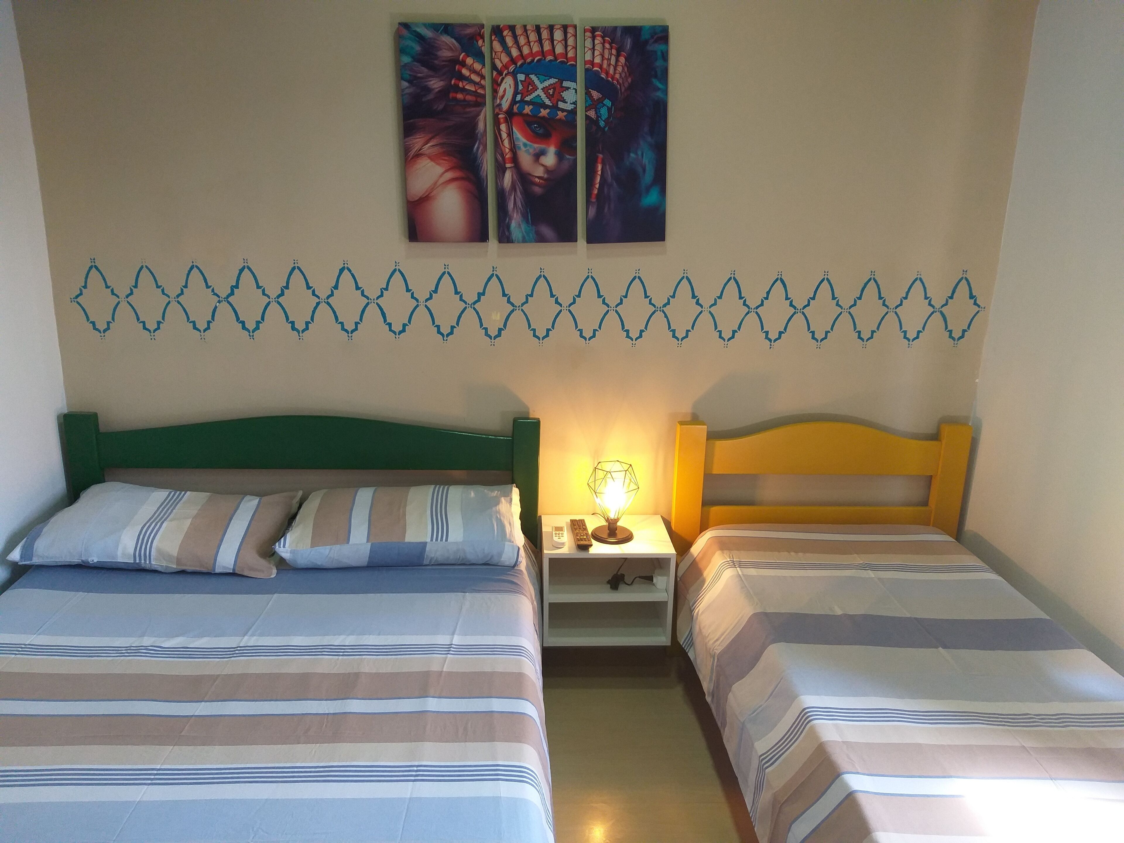 Quarto com duas camas, cada uma com roupa de cama listrada, uma mesa de cabeceira com abajur e um adorno na parede sobre as camas.