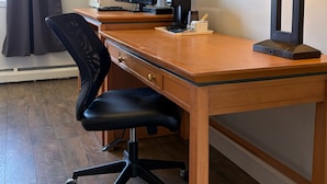 Uma mesa de madeira com um computador, uma cadeira, uma lâmpada e uma janela com cortinas.