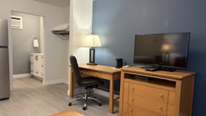 Quarto com escrivaninha de madeira, uma cadeira, televisão, luminária e armário.