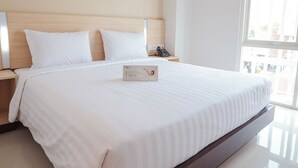 Quarto de hotel moderno com uma cama grande, cabeceira de madeira, mesas de cabeceira e uma janela ampla.