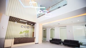 Uma área de recepção de hotel com design moderno, incluindo balcão de atendimento, espaço de estar e vista para o andar superior.