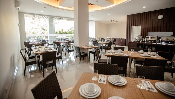 Um restaurante moderno com várias mesas e cadeiras, área de cozinha e janelas grandes que proporcionam luz natural.