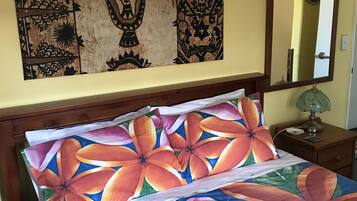 Uma cama com um cobre-leito floral colorido, uma tapeçaria de parede com desenhos detalhados e um espelho sobre uma mesa de cabeceira de madeira.