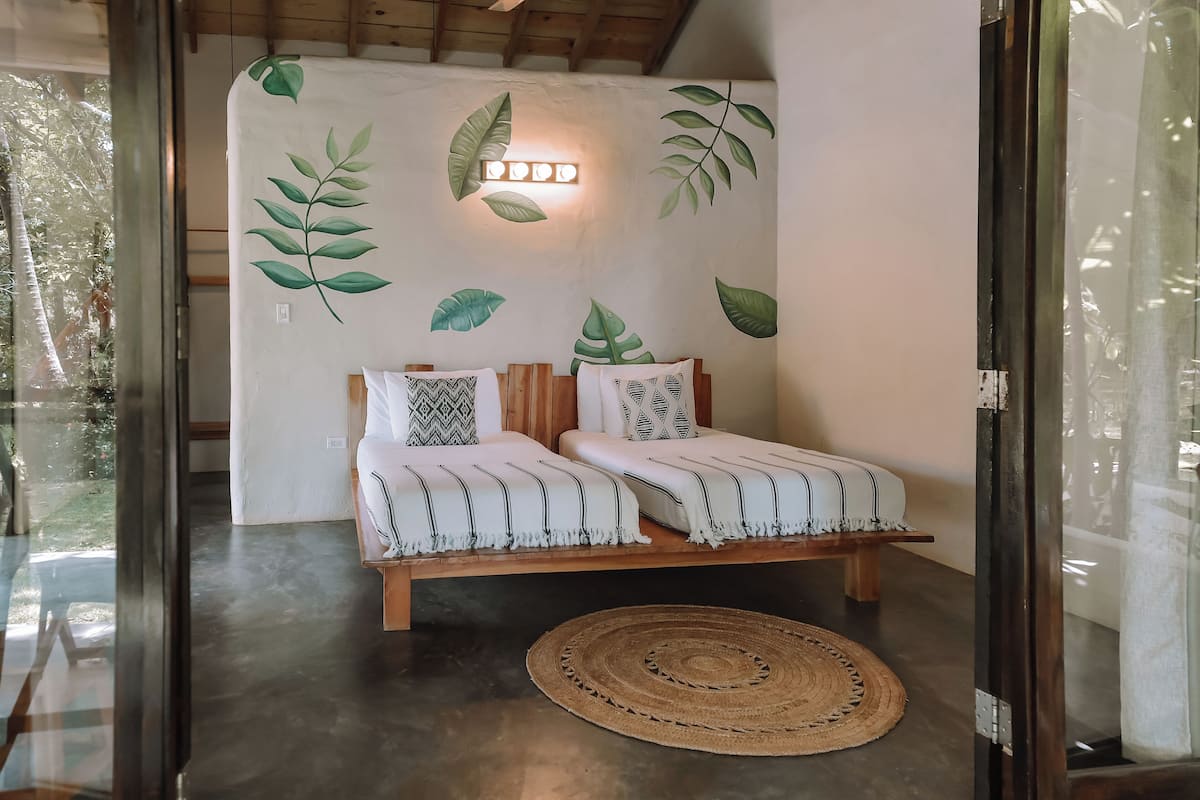 Quarto com uma cama, uma luminária fixada na parede e uma janela grande.