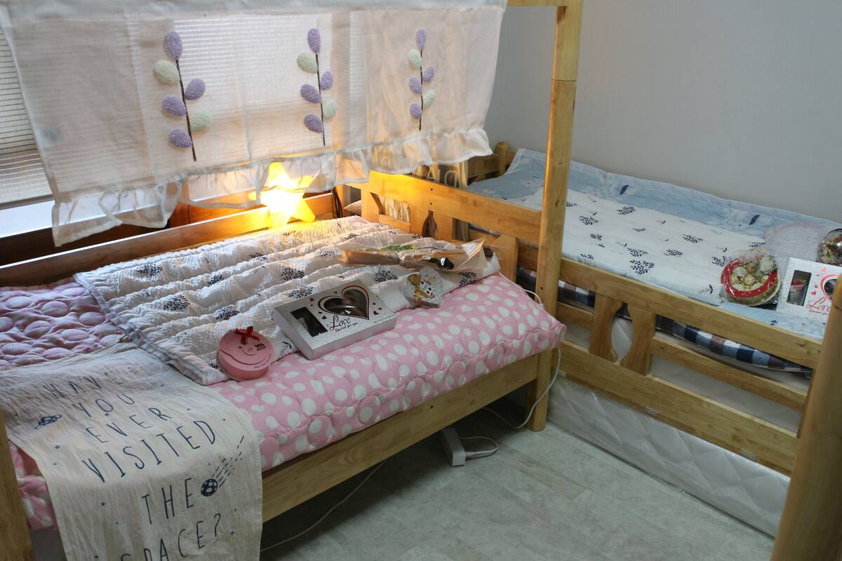 Uma cama beliche com colcha rosa com bolinhas, um cobertor branco com texto e um brinquedo rosa pequeno na cama inferior.