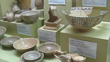 Exposição de cerâmica antiga e esculturas, incluindo tigelas, vasos e um cavalo de cerâmica, cada peça com texto descritivo.