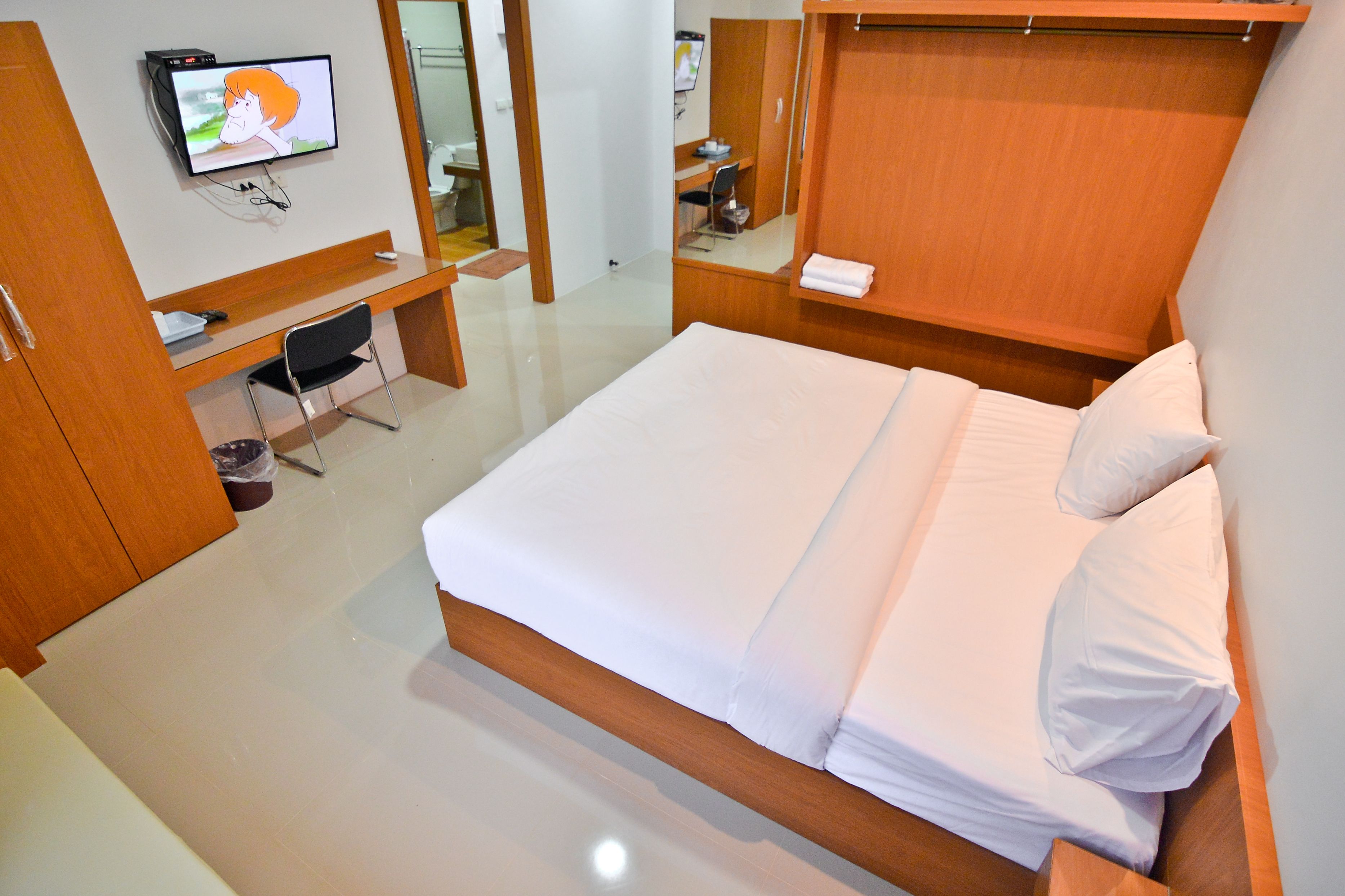 Quarto de hotel com cama, escrivaninha, cadeira e televisão na parede.