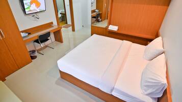 Quarto de hotel com cama, escrivaninha, cadeira e televisão na parede.