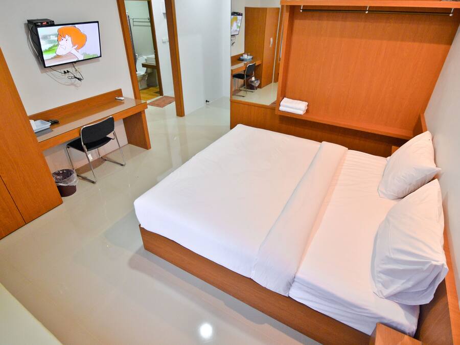 Quarto de hotel com cama, escrivaninha, cadeira e televisão na parede.