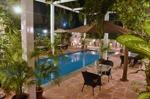 Área interna de piscina com piso de pedra, cercada por plantas em vasos e mobiliário para área externa.
