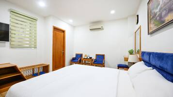 Quarto de hotel com uma cama grande, uma escrivaninha com duas cadeiras, uma televisão e um ar condicionado.