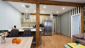 Uma cozinha moderna com vigas de madeira, sala de jantar com mesa e cadeiras e sala de estar com sofá e uma mesinha.