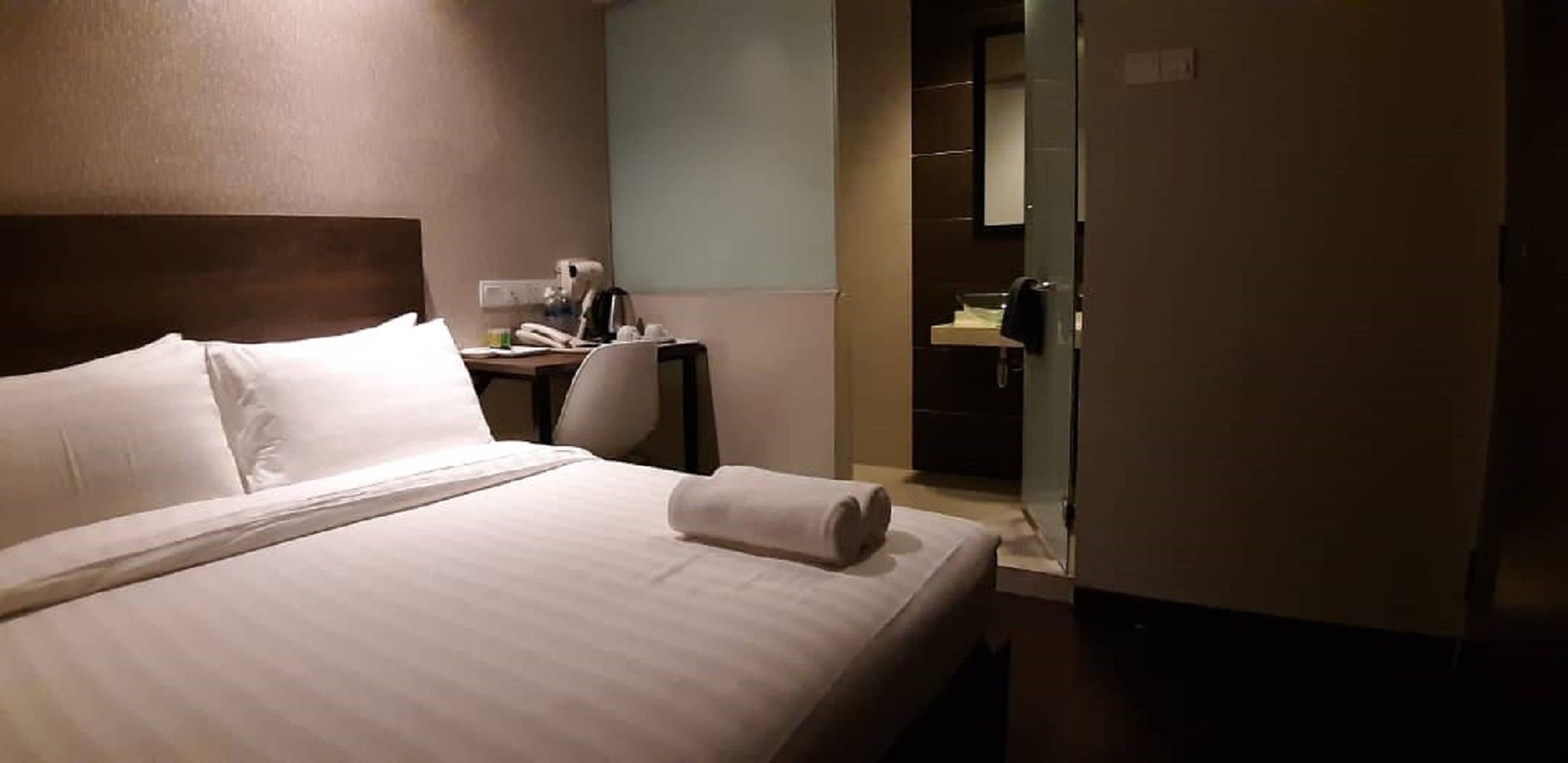 Quarto de hotel com uma cama, uma escrivaninha com telefone e um espelho.