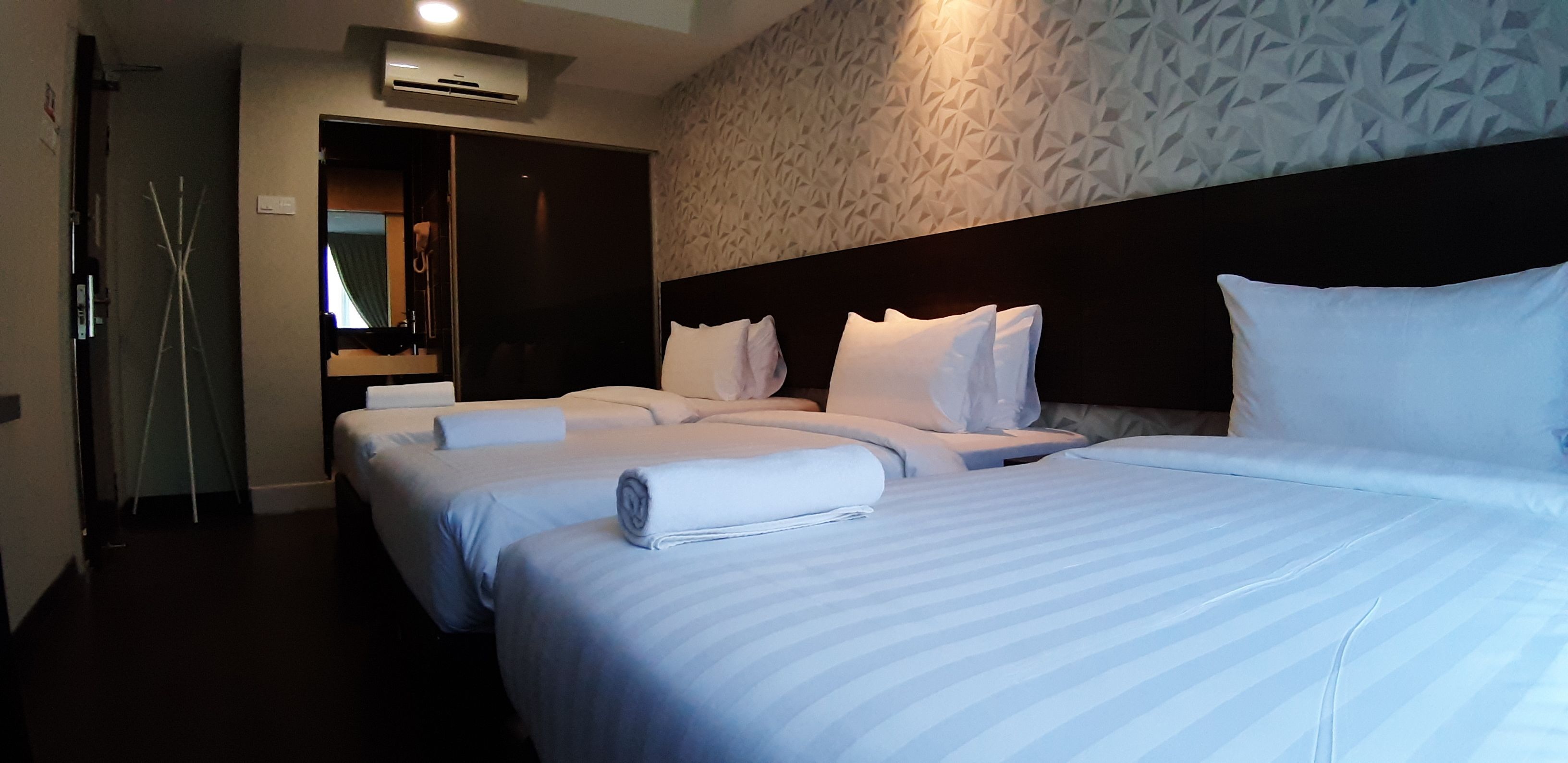 Quarto de hotel com duas camas, cabeceira escura, parede estampada e um espelho.