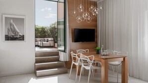 Uma área de jantar moderna com uma mesa de madeira, cadeiras brancas e uma TV fixada na parede.