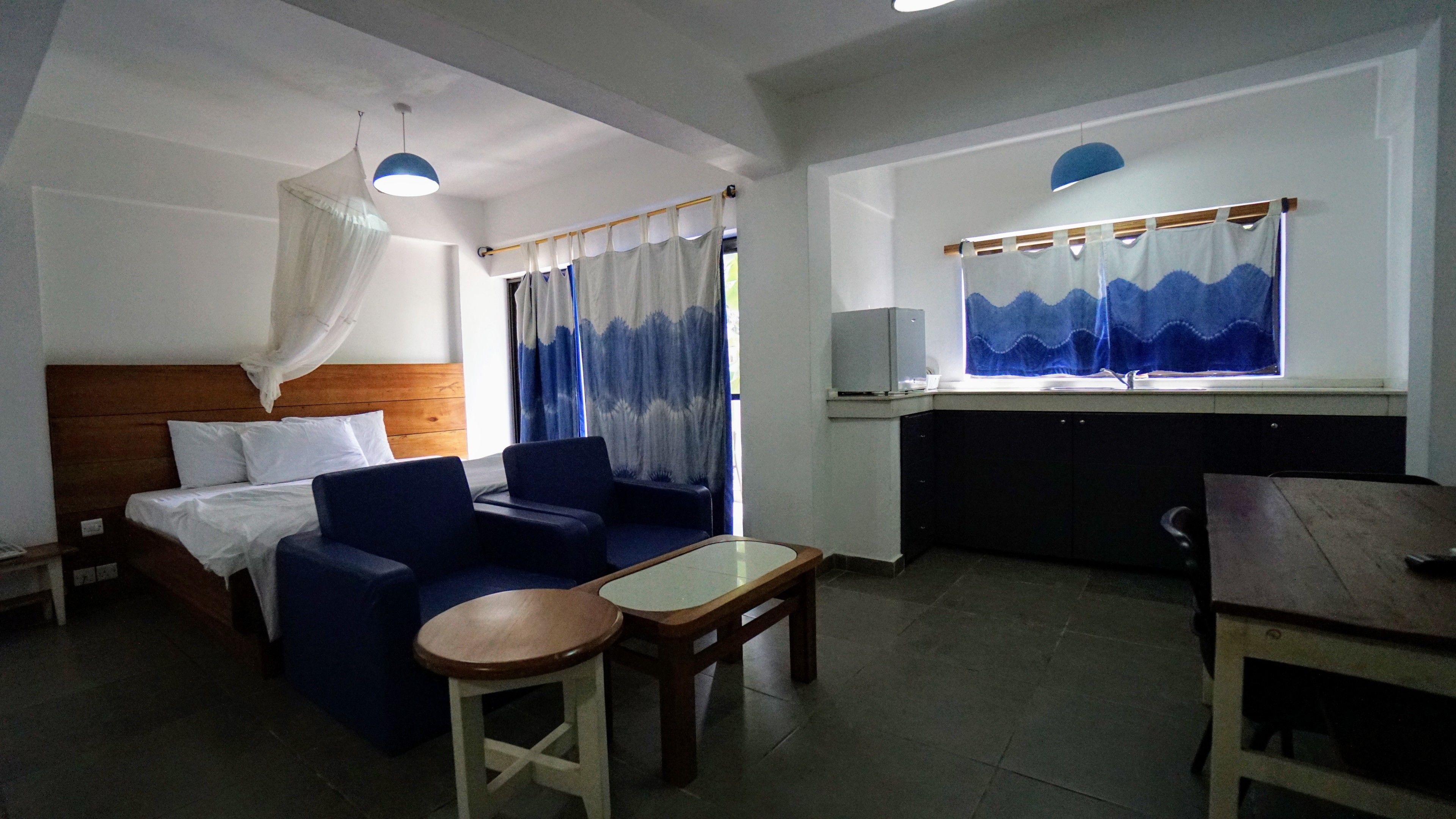 Quarto de hotel com cama, sofá, mesa pequena e cozinha compacta.