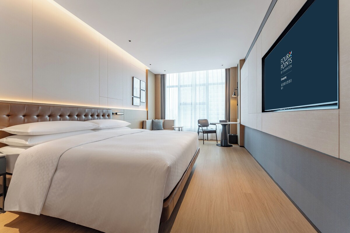 Quarto de hotel moderno com uma cama grande, uma escrivaninha e uma TV exibindo "FOUR POINTS BY SHENTON".