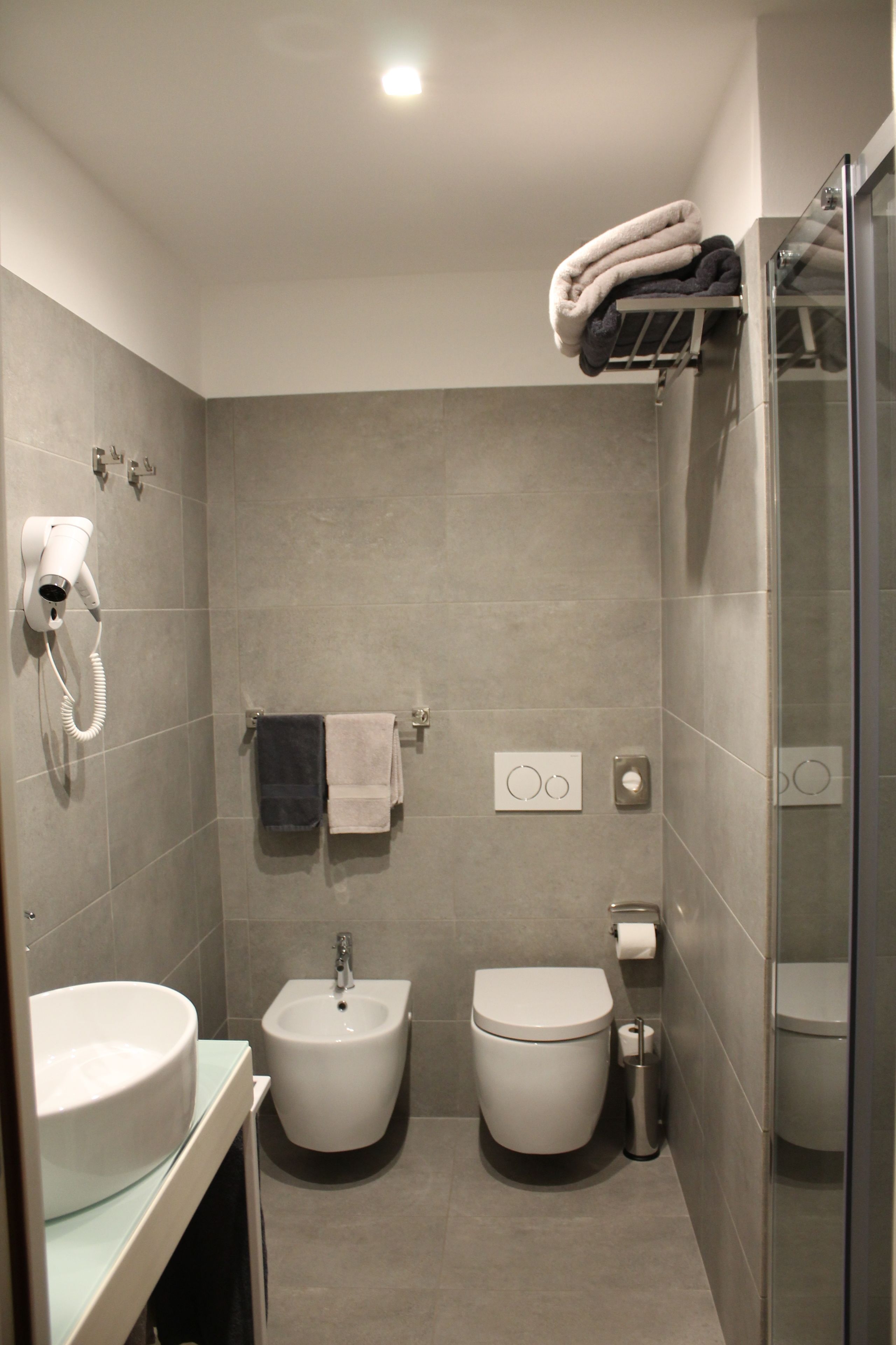 Uma casa de banho moderna com bidé, duas sanitas, lavatório, secador de cabelo e barra de toalhas.