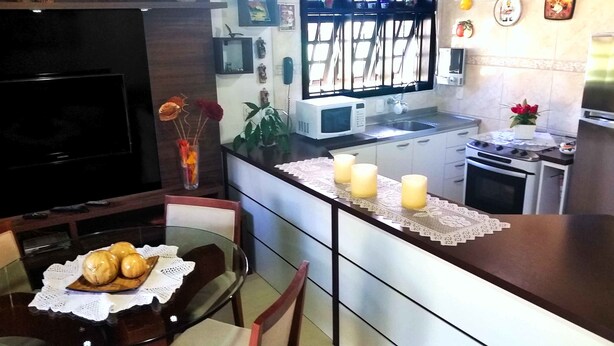 Uma cozinha moderna com micro-ondas, fogão e pia. Há uma mesa de jantar com toalha rendada e velas.