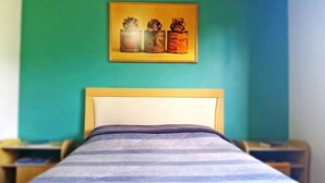 Uma cama com colcha listrada, cabeceira de madeira e um quadro com enlatados na parede.
