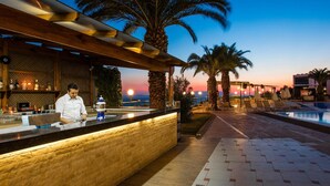 Uma área de bar ao ar livre com piscina e palmeiras, com vista para o pôr do sol.