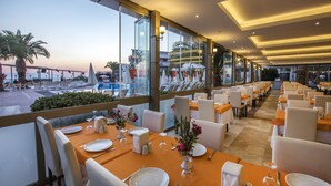 Restaurante com mesas preparadas para refeições, grandes janelas com vista para a praia e design de interiores moderno.