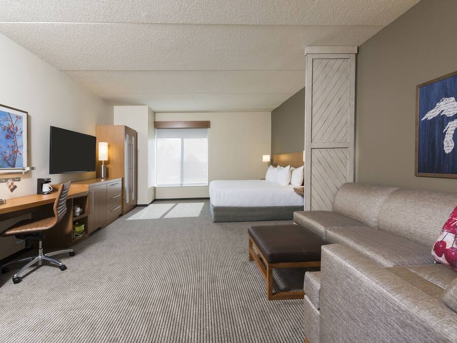 Quarto de hotel com cama, sofá, escrivaninha com cadeira, televisão e janela.