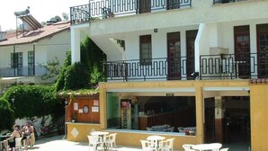 Um edifício de dois andares com área de café no andar térreo e mesas ao ar livre.
