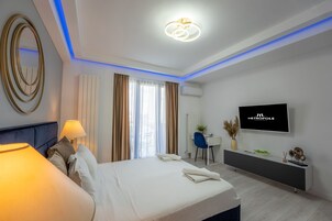 Quarto de hotel moderno com cama, abajur, televisão, escrivaninha e vista para o exterior.