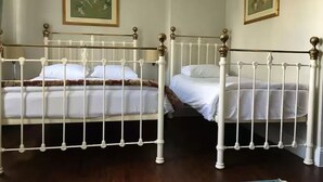 Quarto com duas camas, cada uma com roupa de cama e estrutura de metal brancas. Há duas imagens emolduradas nas paredes.