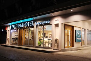 Exterior moderno de hotel com placa visível, grandes janelas e entrada bem iluminada.