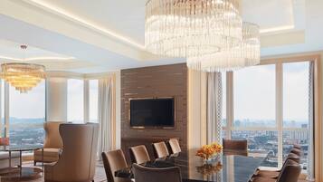 Uma sala de jantar ampla com uma mesa grande e cadeiras, um lustre moderno e uma televisão fixada em uma parede de pedra.