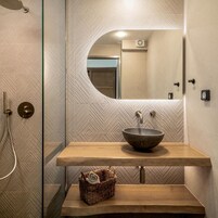 Casa de banho com toucador de madeira, lavatório suspenso, área de duche e parede com padrão herringbone.