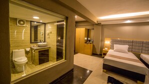 Quarto de hotel com um espelho grande, pia, sanita, cama, mesa de cabeceira e guarda-roupa.