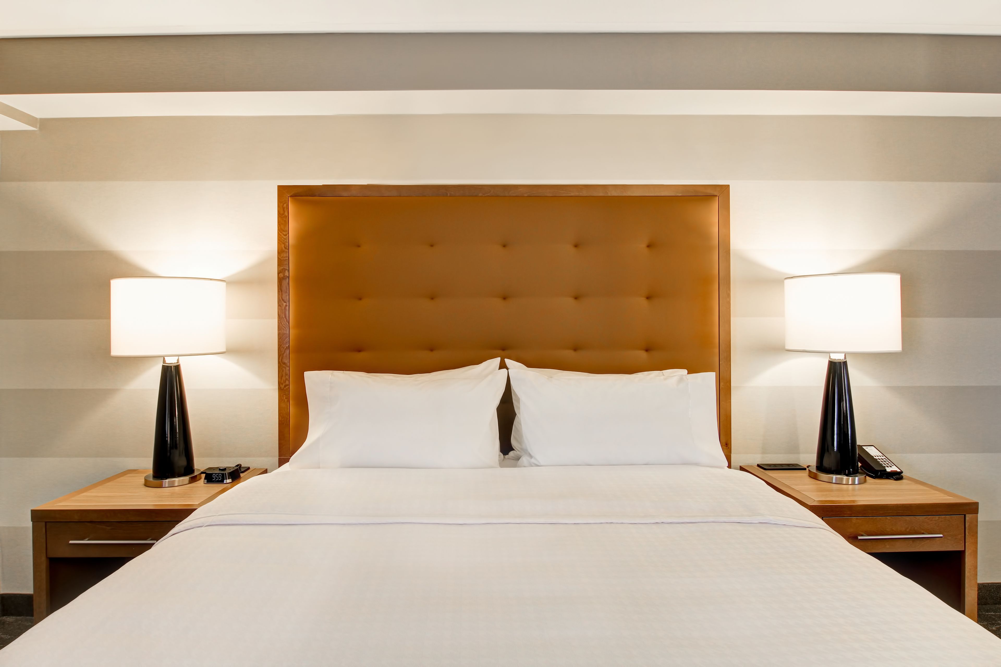 Quarto de hotel com uma cama grande, duas mesas de cabeceira e duas luminárias.