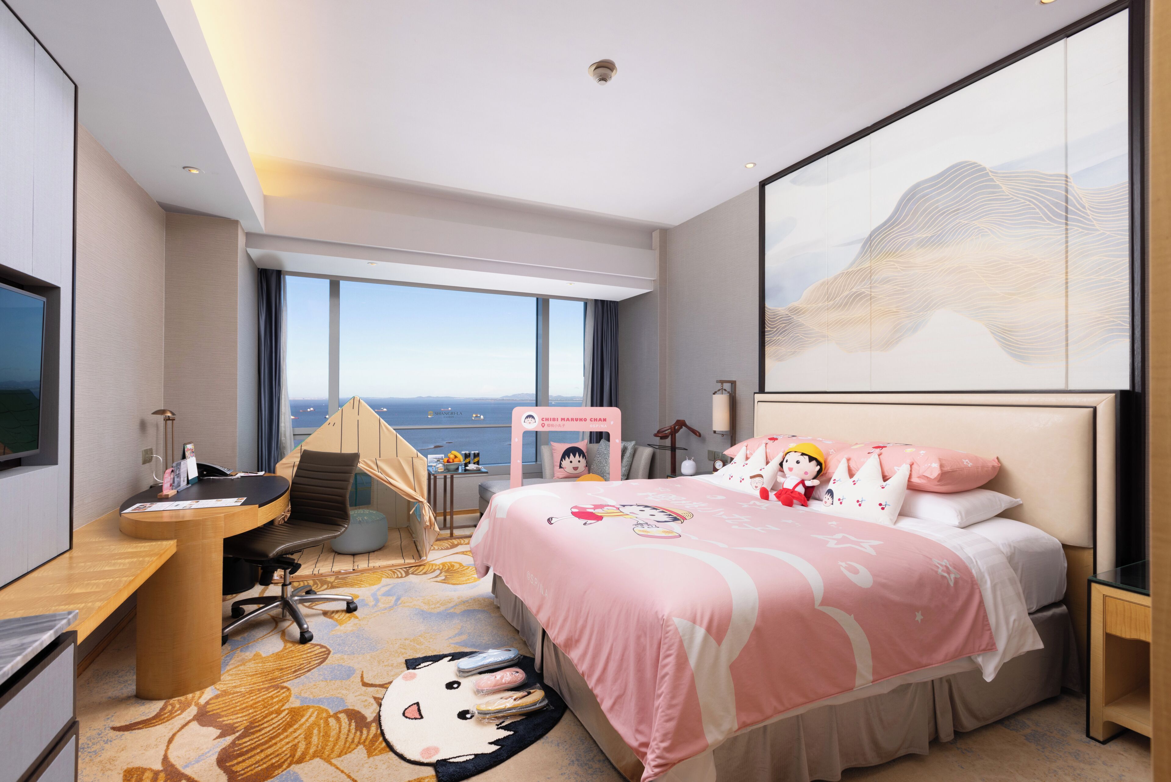 Quarto de hotel moderno com uma cama grande, escrivaninha, cadeira, vista da cidade e uma obra de arte de grandes dimensões na parede.