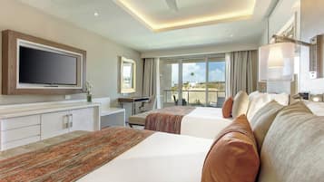 Quarto de hotel com duas camas, televisão, escrivaninha e uma janela grande com vista para a praia.