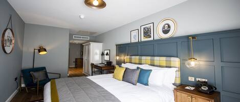 Quarto de hotel com cama, mesa de cabeceira, luminária e guarda-roupa.