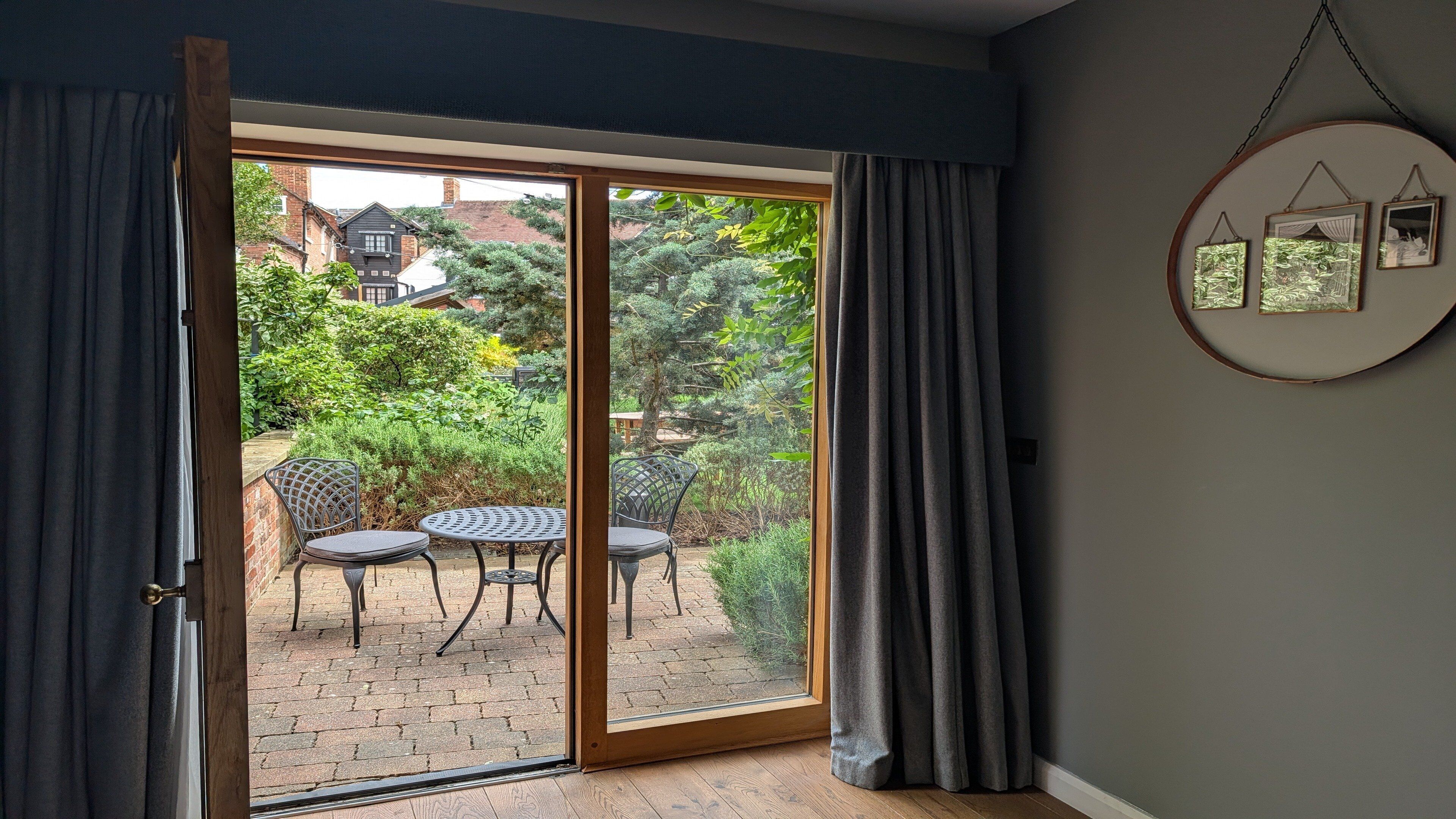 Quarto com porta de vidro deslizante para um pátio com mesa e cadeiras, decoração circular na parede e vista para uma área residencial.
