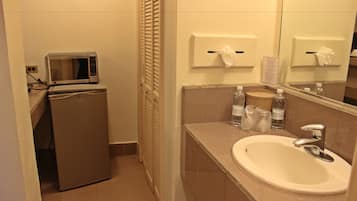 Casa de banho de hotel compacta com lavatório, espelho e um micro-ondas num pequeno armário.