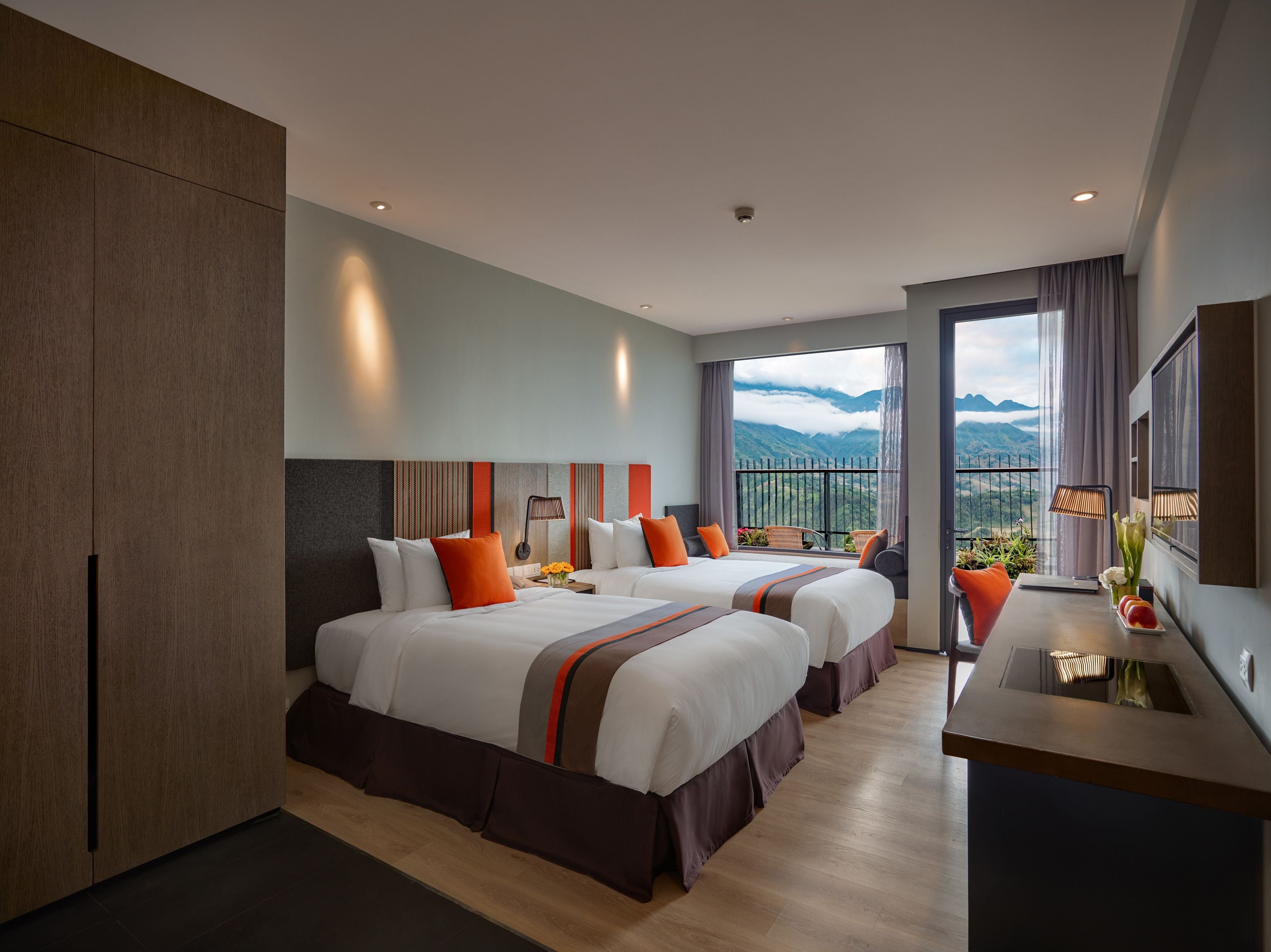Quarto de hotel com duas camas, varanda com vista para as montanhas e escrivaninha com luminária.