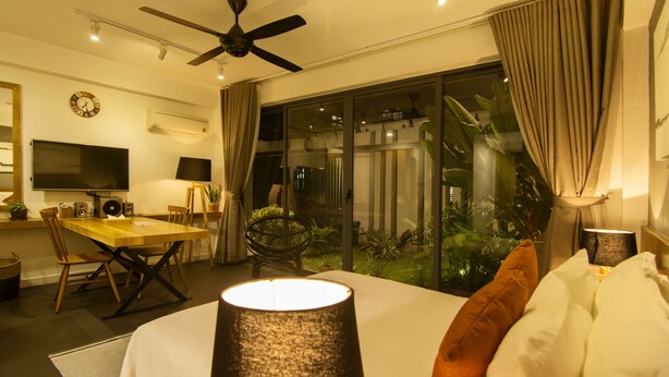 Quarto de hotel com cama, secretária, cadeira, televisão e varanda com plantas.