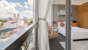 Quarto de hotel moderno com uma grande janela, uma cama, uma escrivaninha e vista para a paisagem urbana.