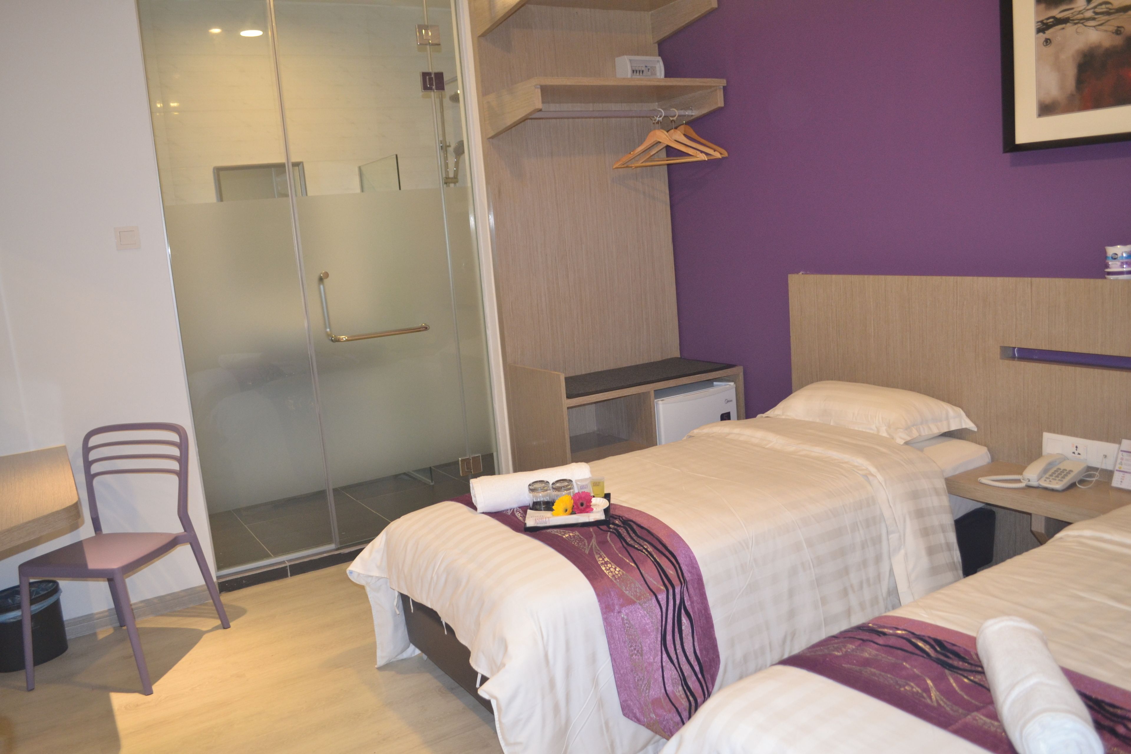 Quarto de hotel com duas camas, área de chuveiro, escrivaninha com telefone e uma cadeira.